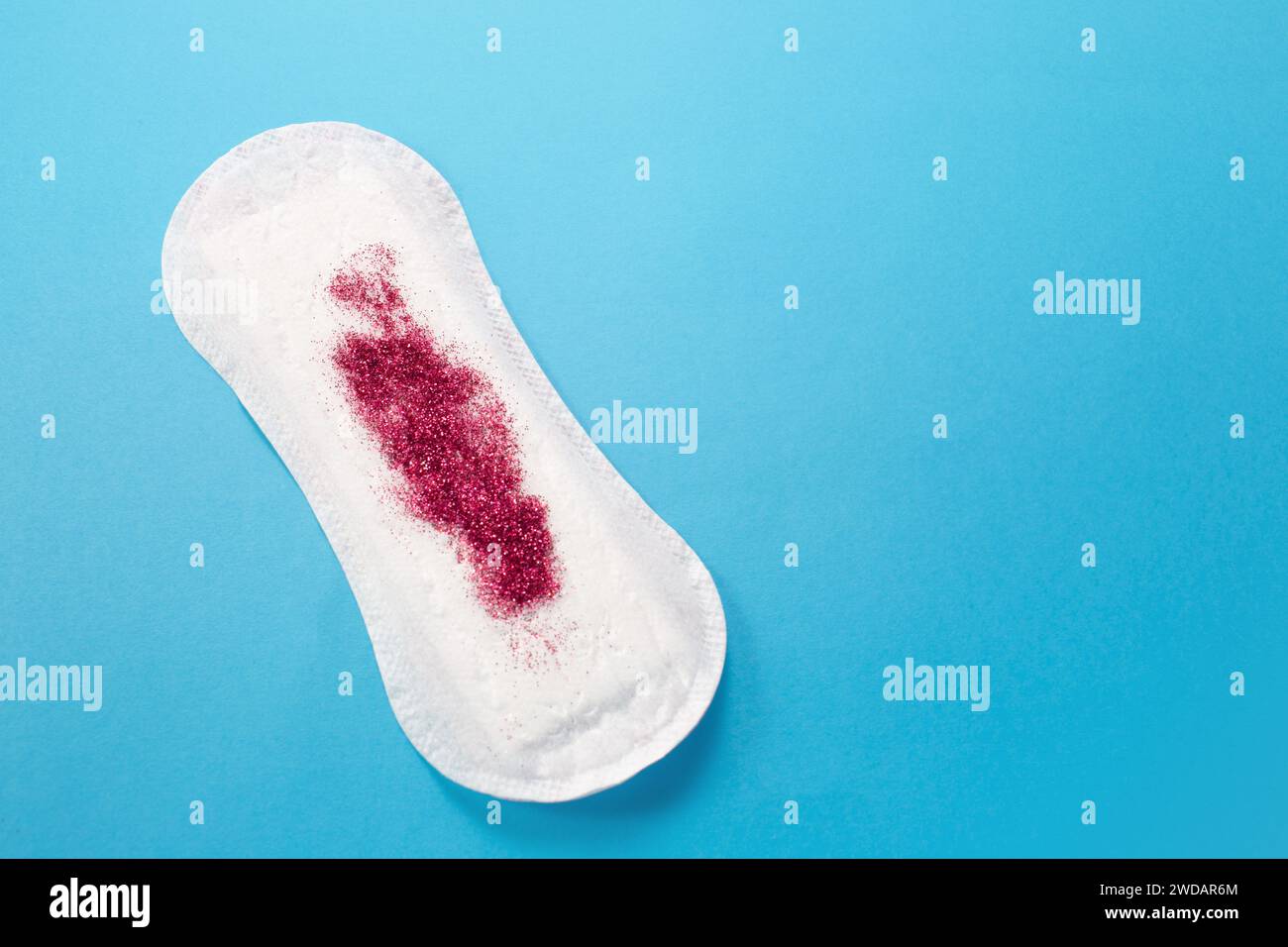 Feminine hygiene pad with red glitter on blue background. First ...