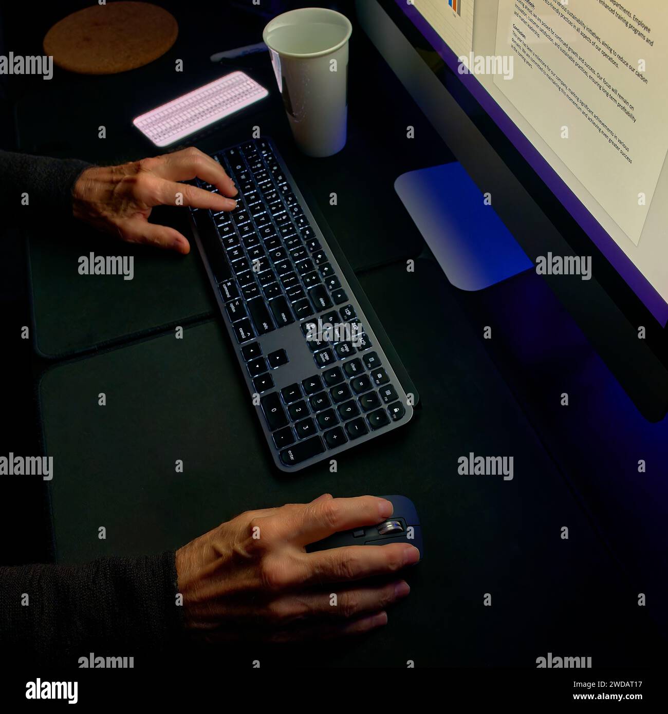 A professional's desk at night, with the focus on hands typing and a ...