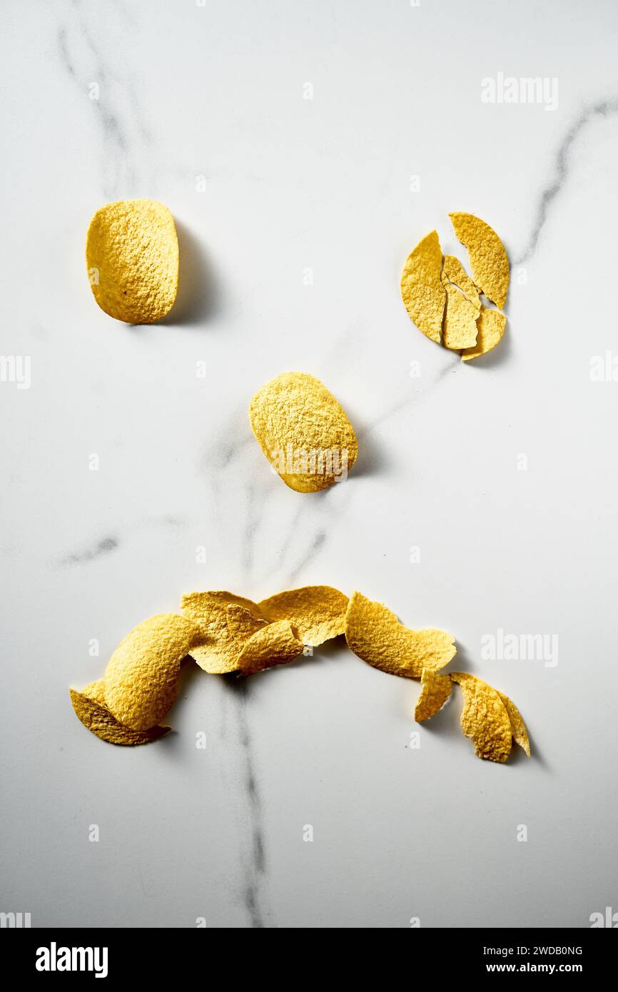 Potato chips shaped like a sad smiley face with with one broken eye on ...