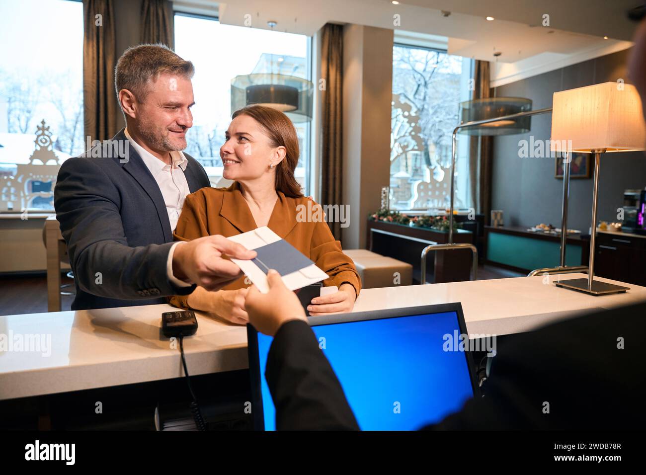Man giving passport to receptionist and looking at woman at desk in ...