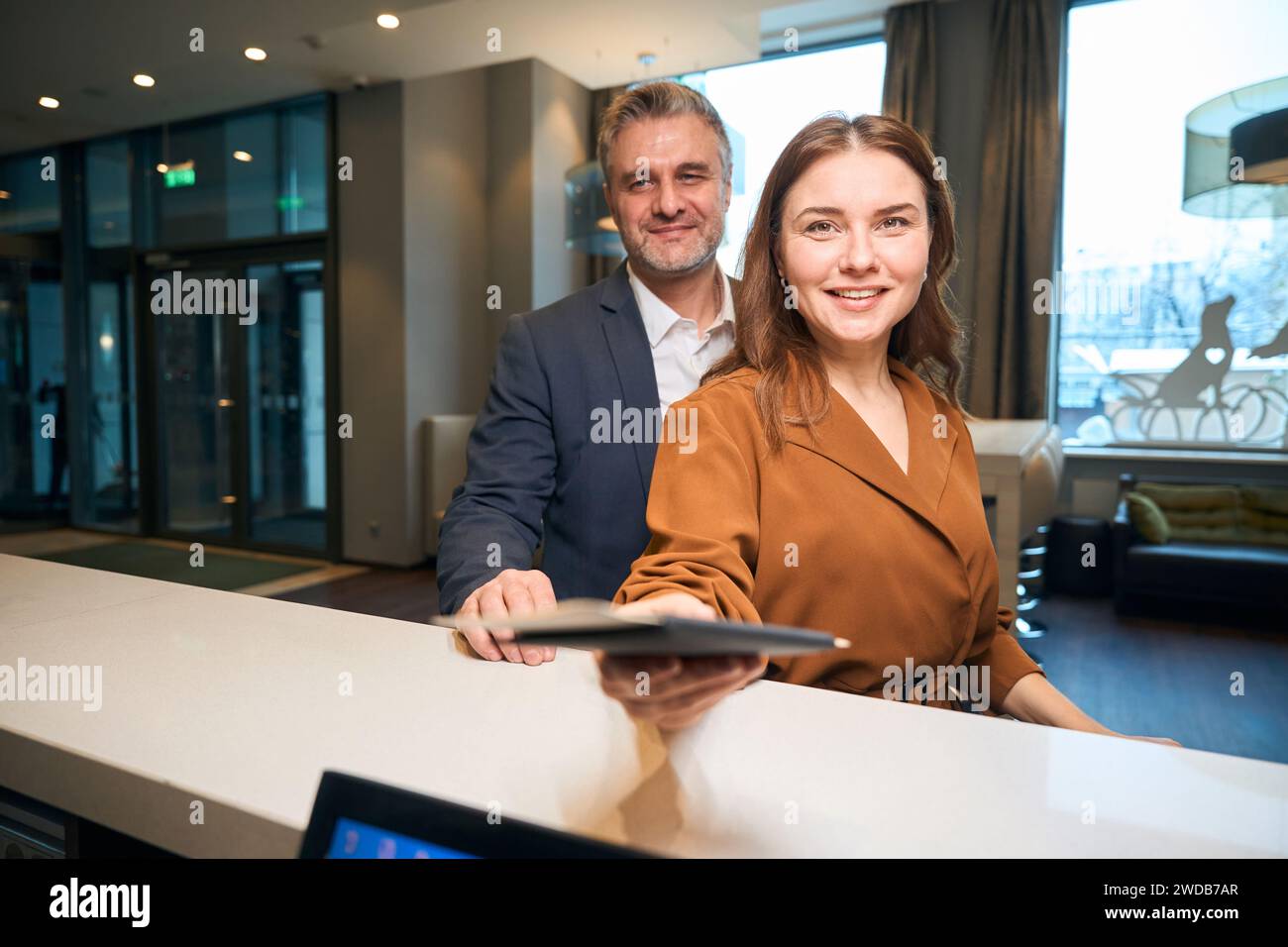 Woman giving passport at reception desk near her man standing in hotel ...