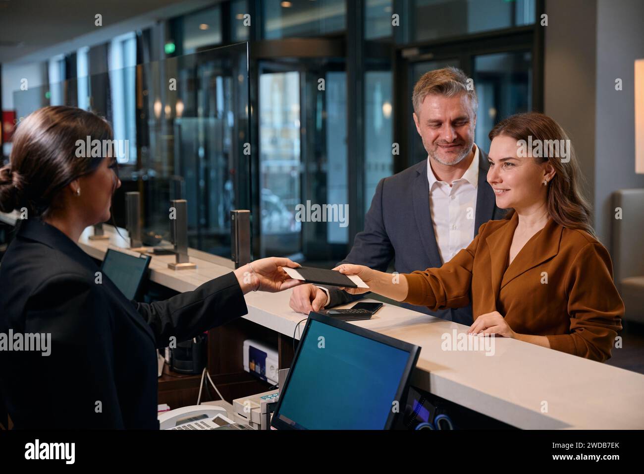Woman giving passport to female european receptionist near man in hotel ...