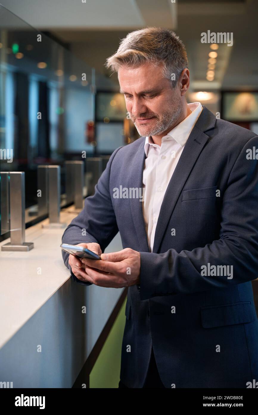 Focused adult businessman using smartphone at reception desk in hotel ...