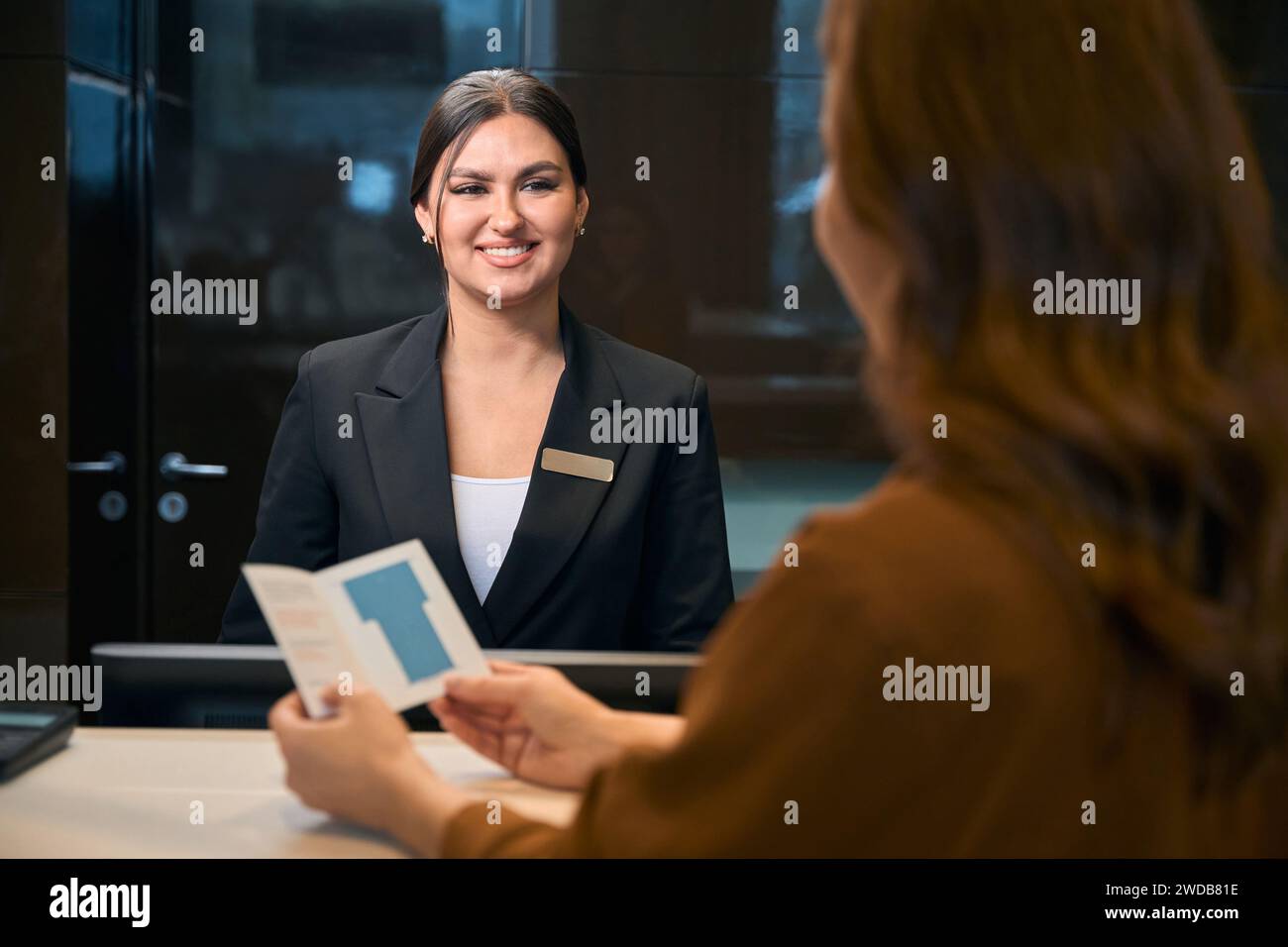Woman with passport and receptionist looking at each other at reception ...