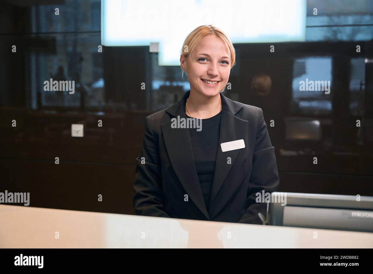 Female receptionist wearing uniform looking at camera at reception desk ...