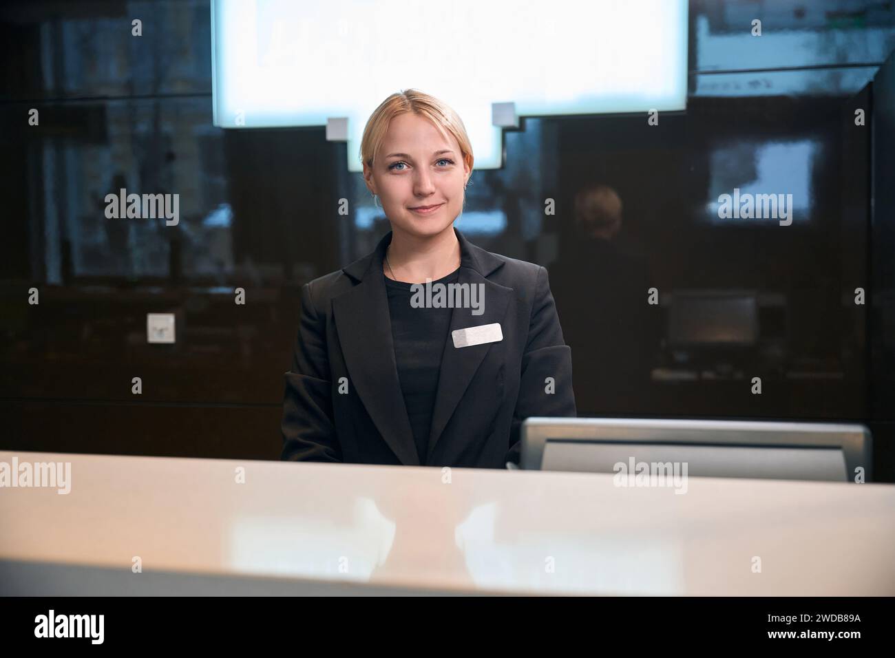Portrait of receptionist looking at camera at reception desk in hotel ...