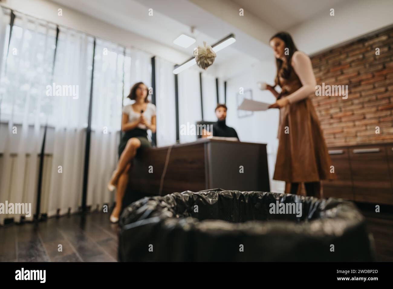 Three people having fun at work. Male person throwing garbage at the ...