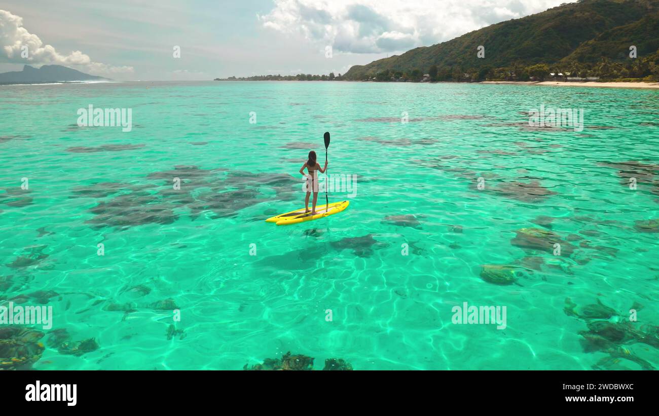 Woman standing on yellow sup board with paddle. Crystal turquoise water ...