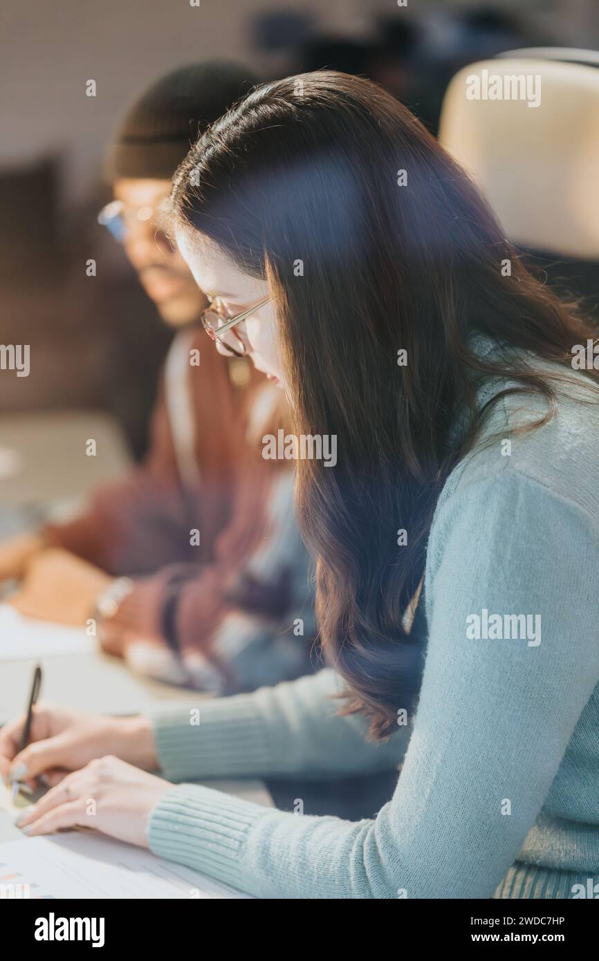 A young female adult with glasses concentrates on writing notes during ...