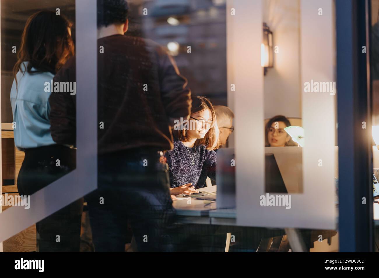 Dedicated team working late hours in modern office space viewed through ...