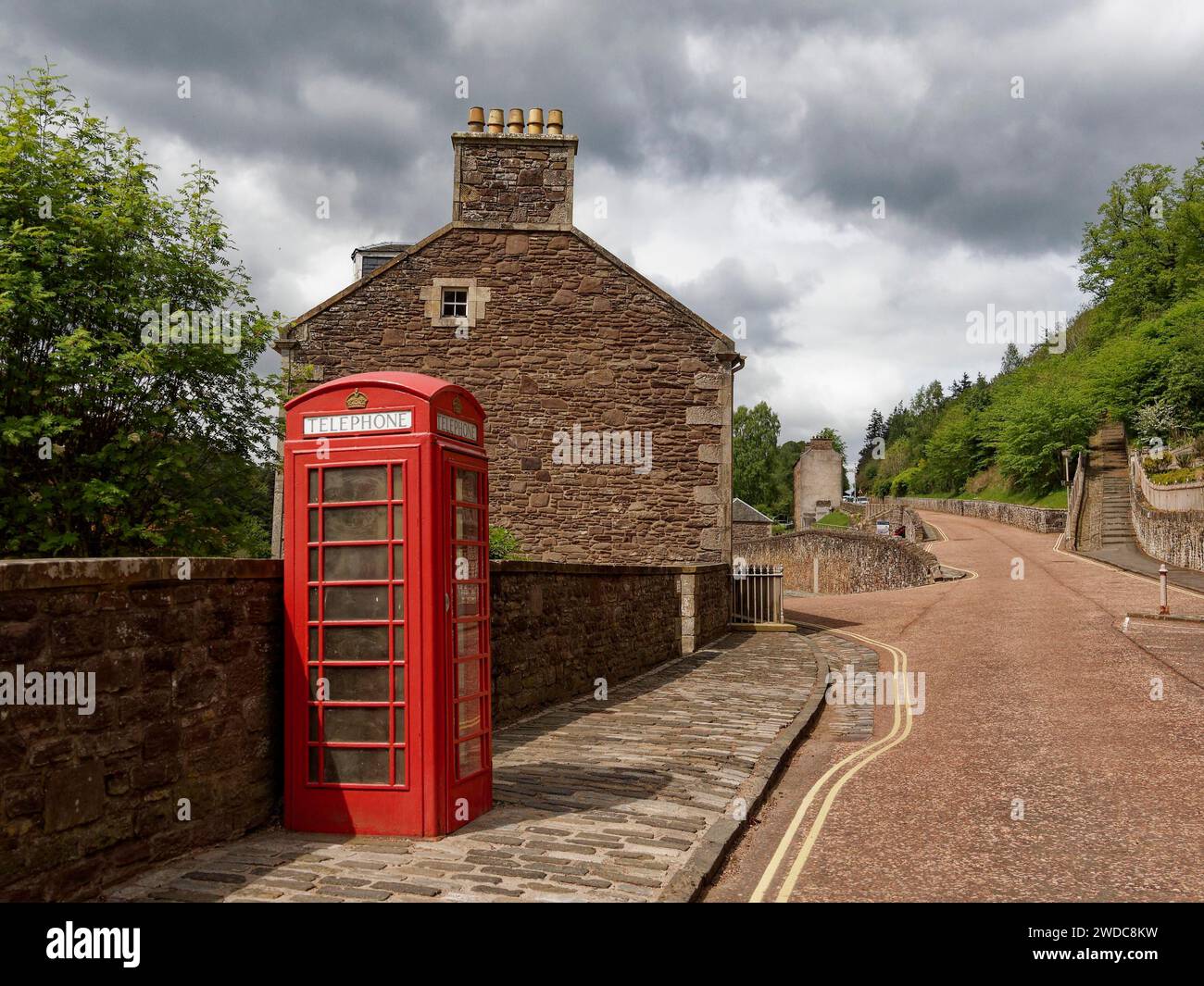 A classic red telephone box in front of an old stone house on a quiet ...