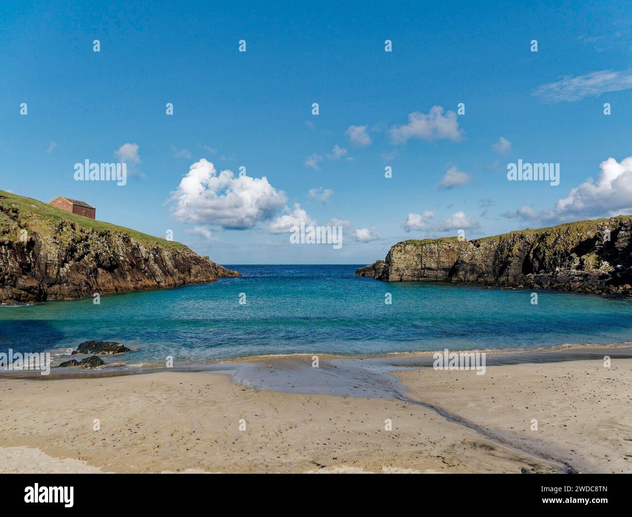 A quiet beach cove with clear blue water surrounded by grassy cliffs ...