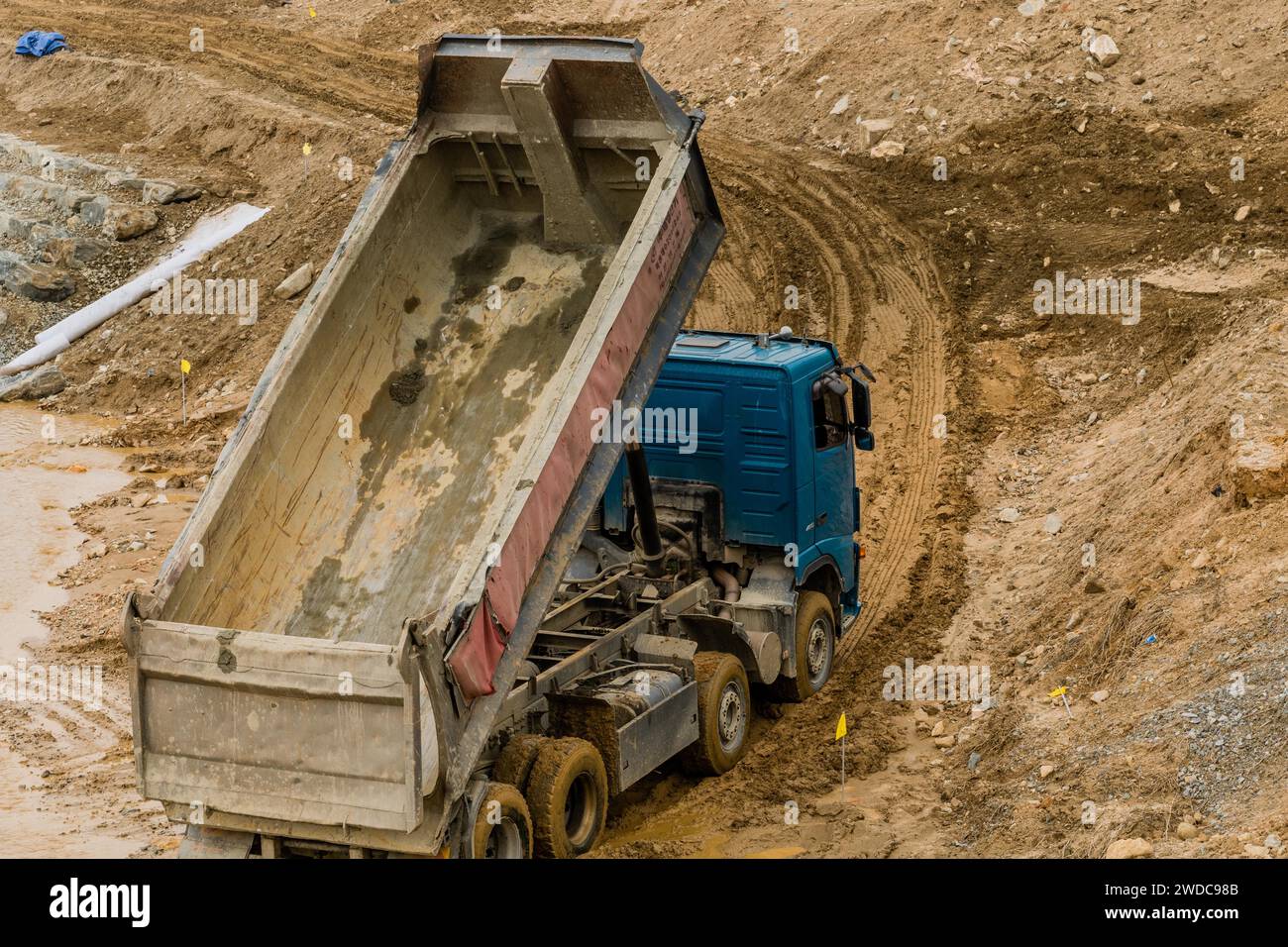 Blue dump truck with raised bed in muddy ravine at new construction ...