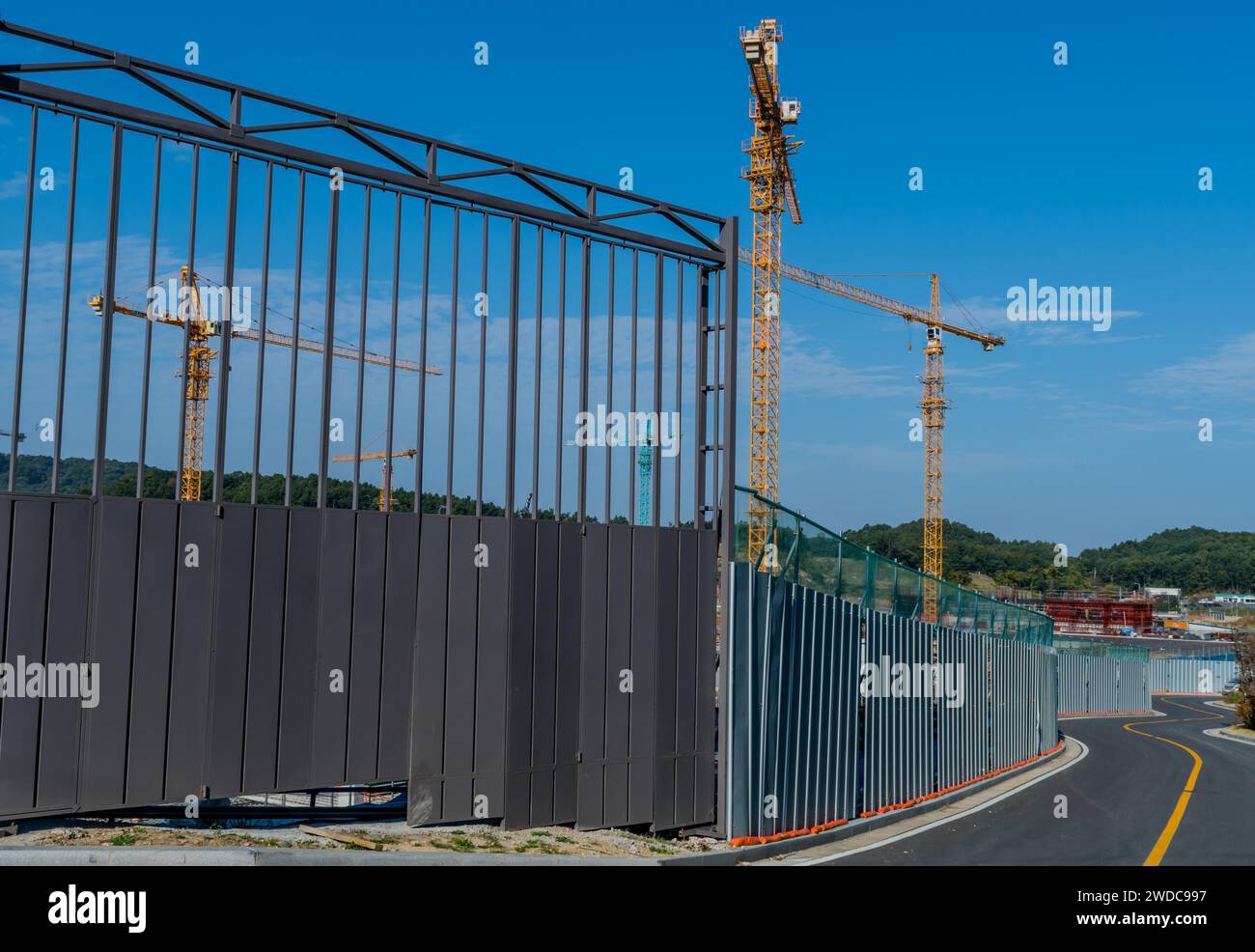 Yellow construction cranes behind gray fence at new construction site ...