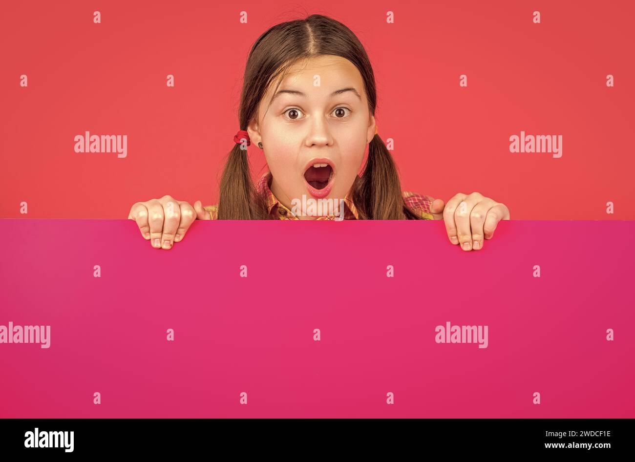 amazed kid behind blank pink paper with copy space for advertisement ...