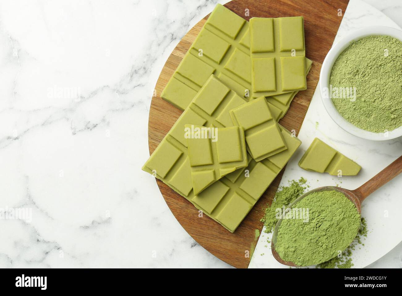 Pieces of tasty matcha chocolate bar and powder on white marble table ...