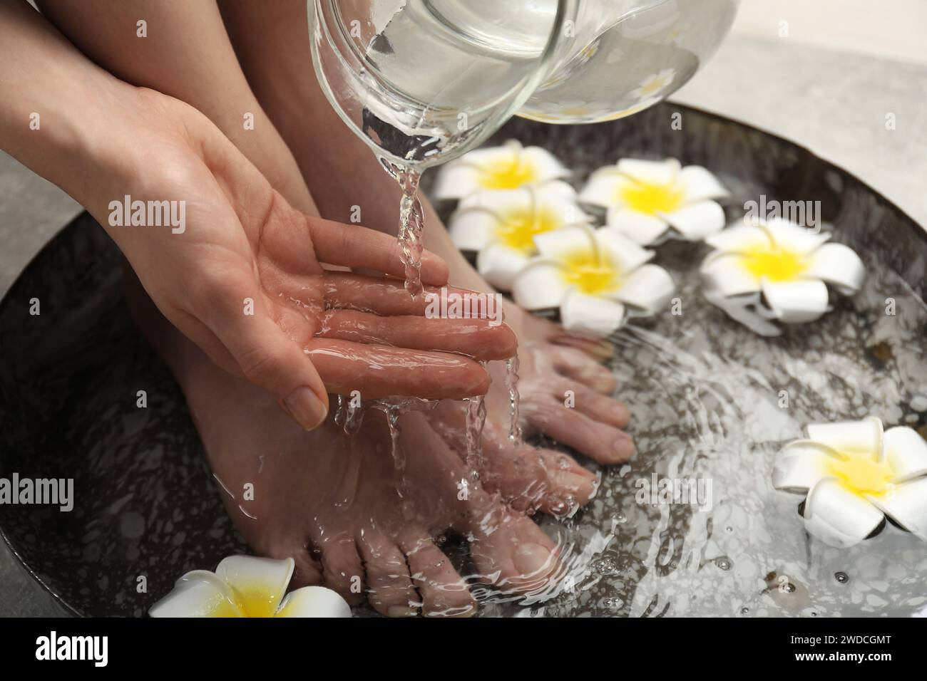 Woman pouring water onto hand while soaking her feet in bowl, closeup ...