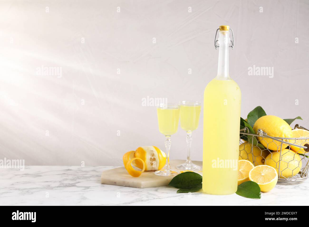 Tasty limoncello liqueur, lemons and green leaves on white marble table ...