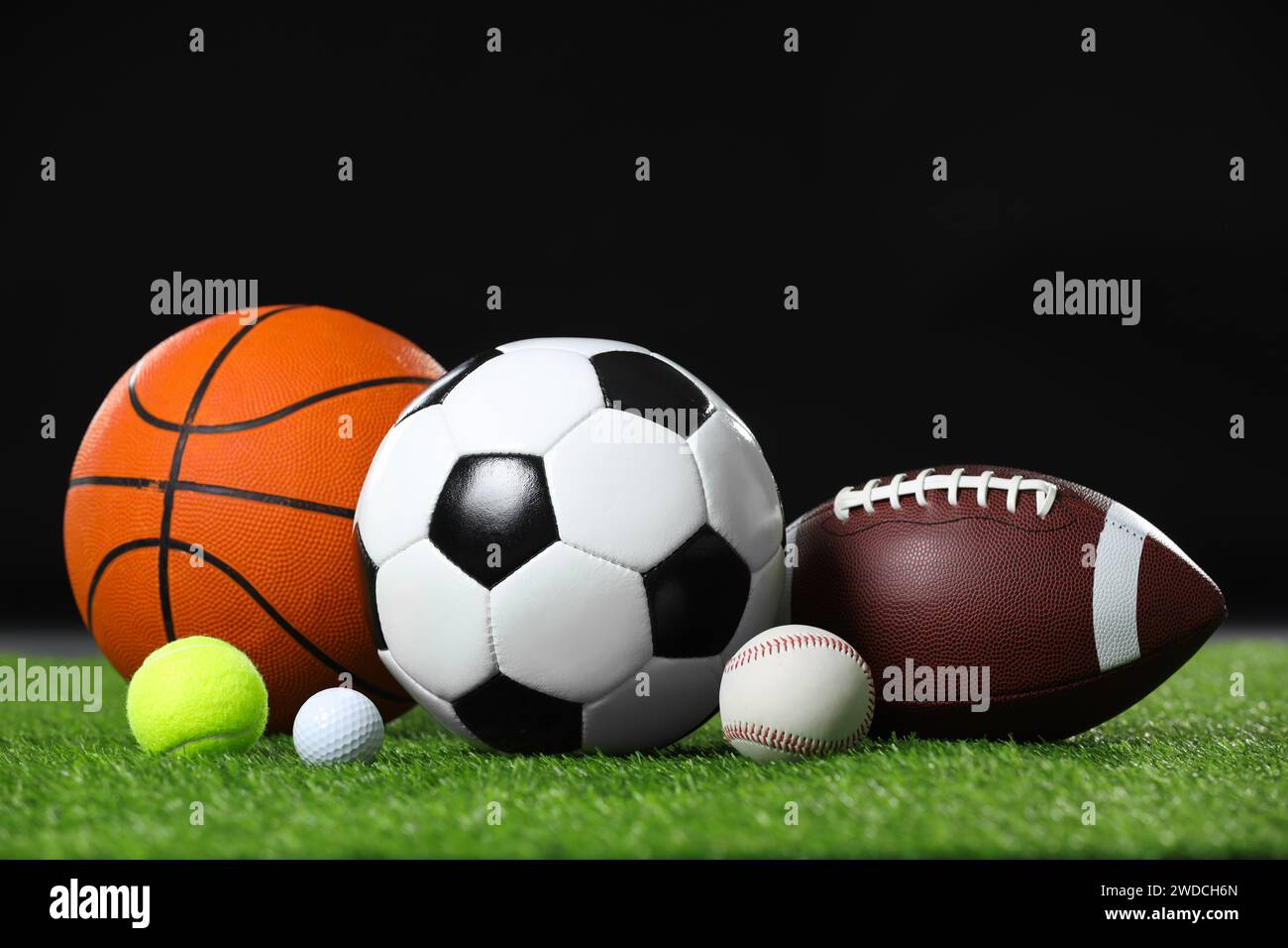 Many different sports balls on green grass against black background ...