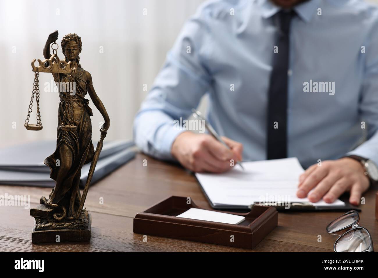 Lawyer working at wooden table in office, focus on statue of Lady ...