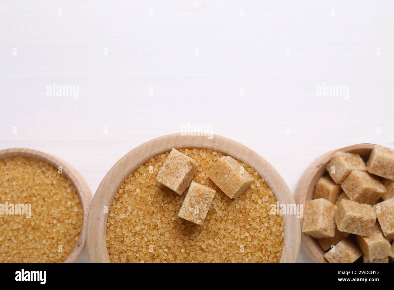 Different types of brown sugar in bowls on white table, flat lay. Space ...