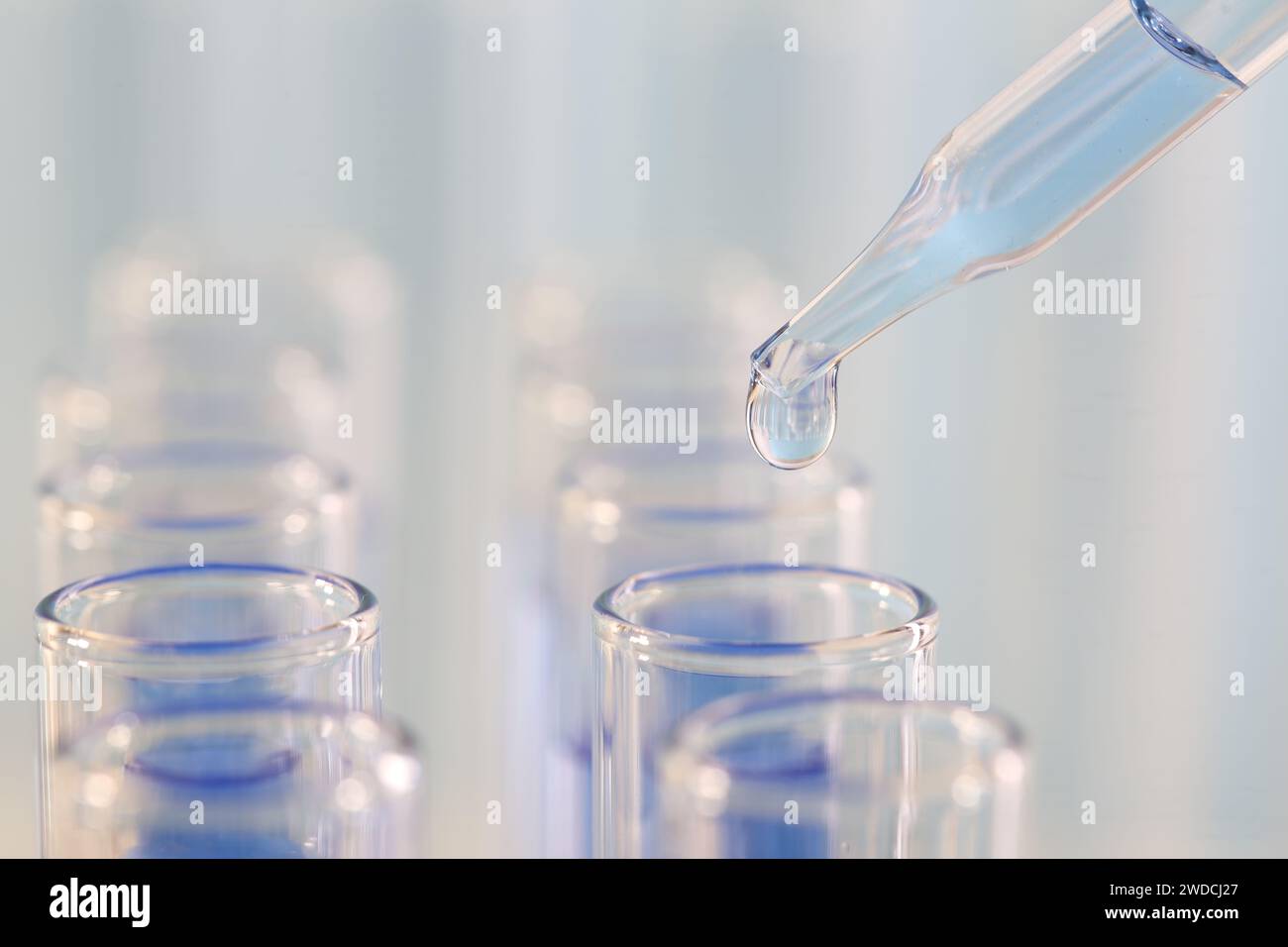 Laboratory analysis. Dripping light blue liquid from pipette into glass ...