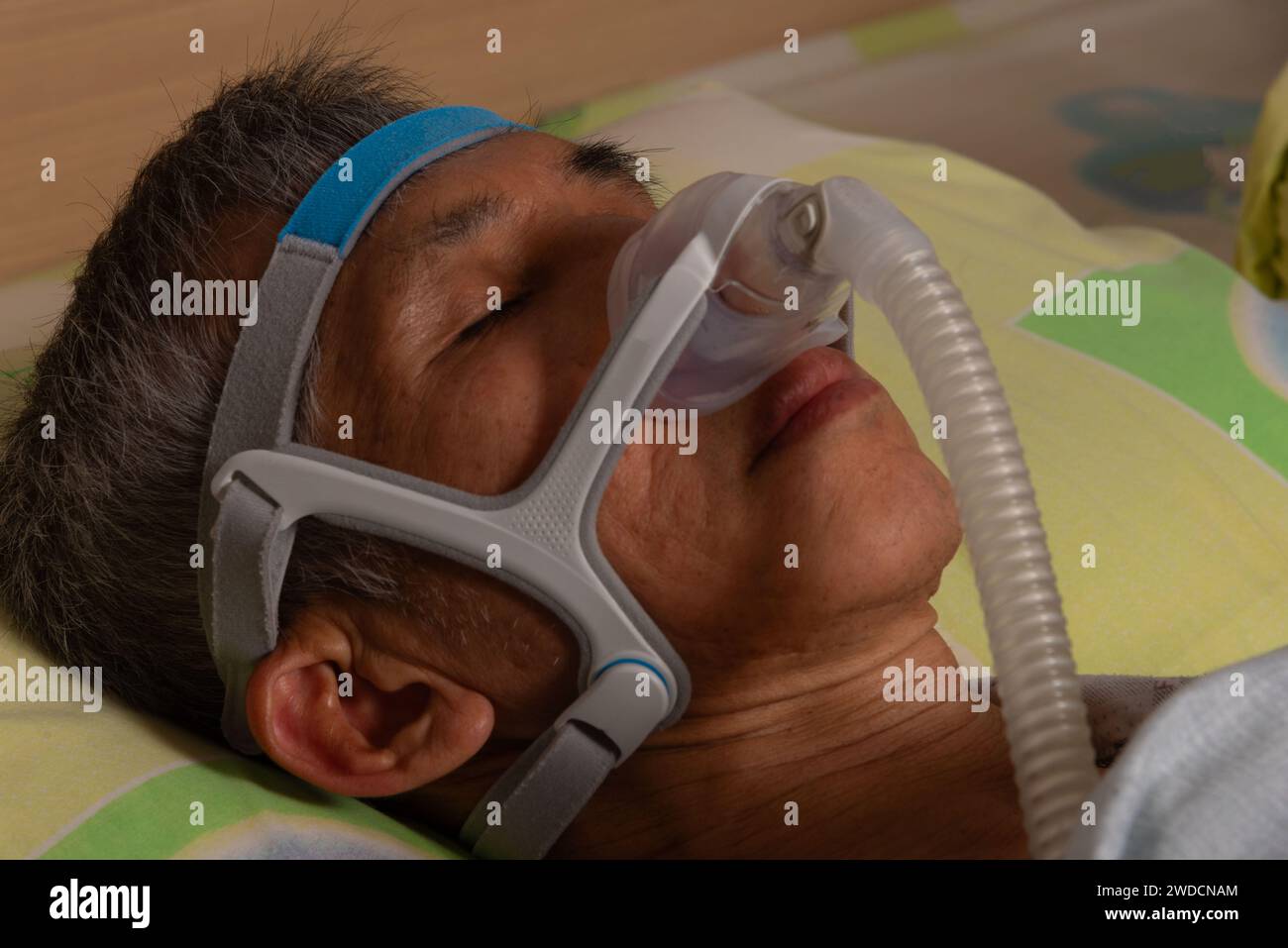 An Asian oder male asleep with CPAP machine for sleep apnea treatment ...