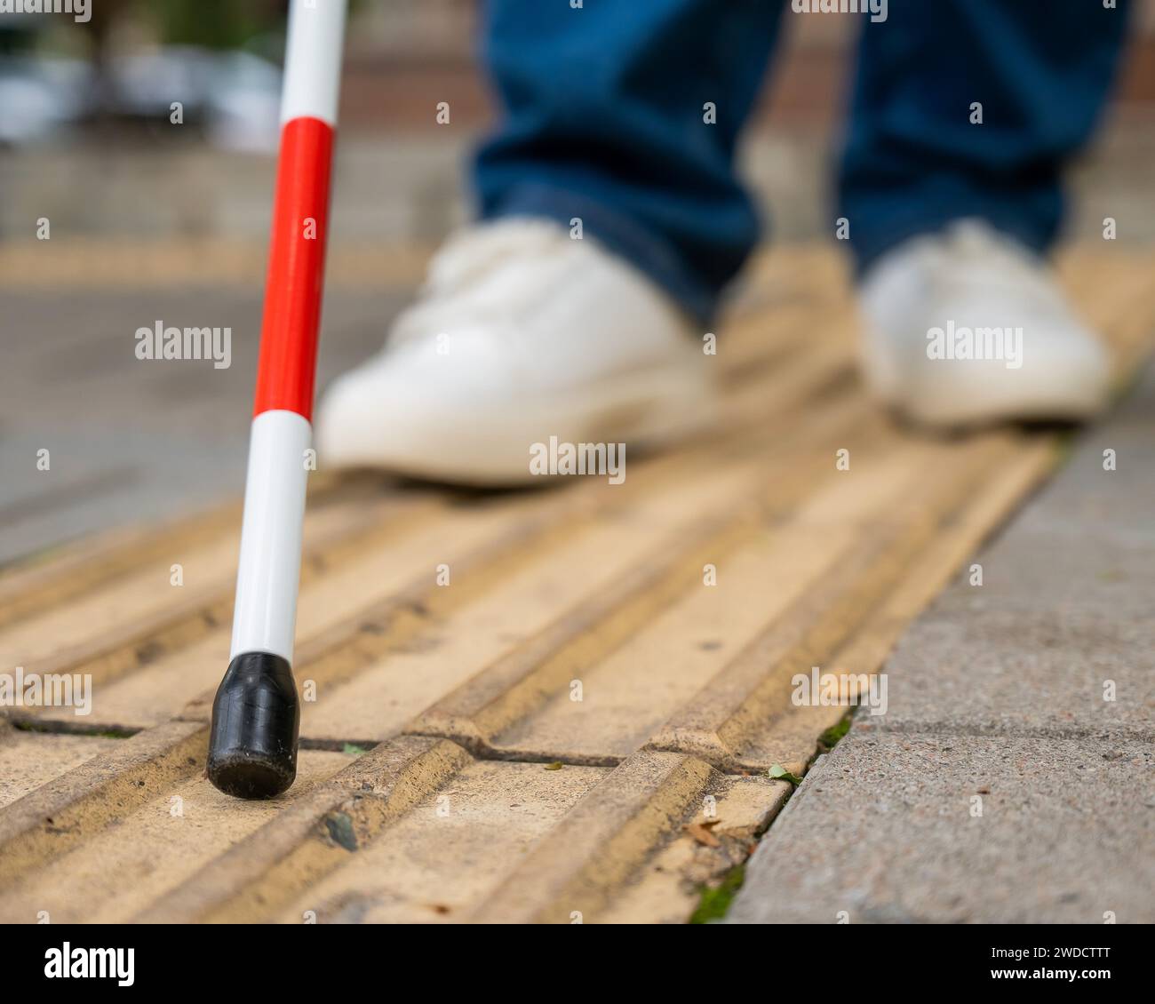 A blind woman walks on the street on tactile yellow tiles. Focus on the ...
