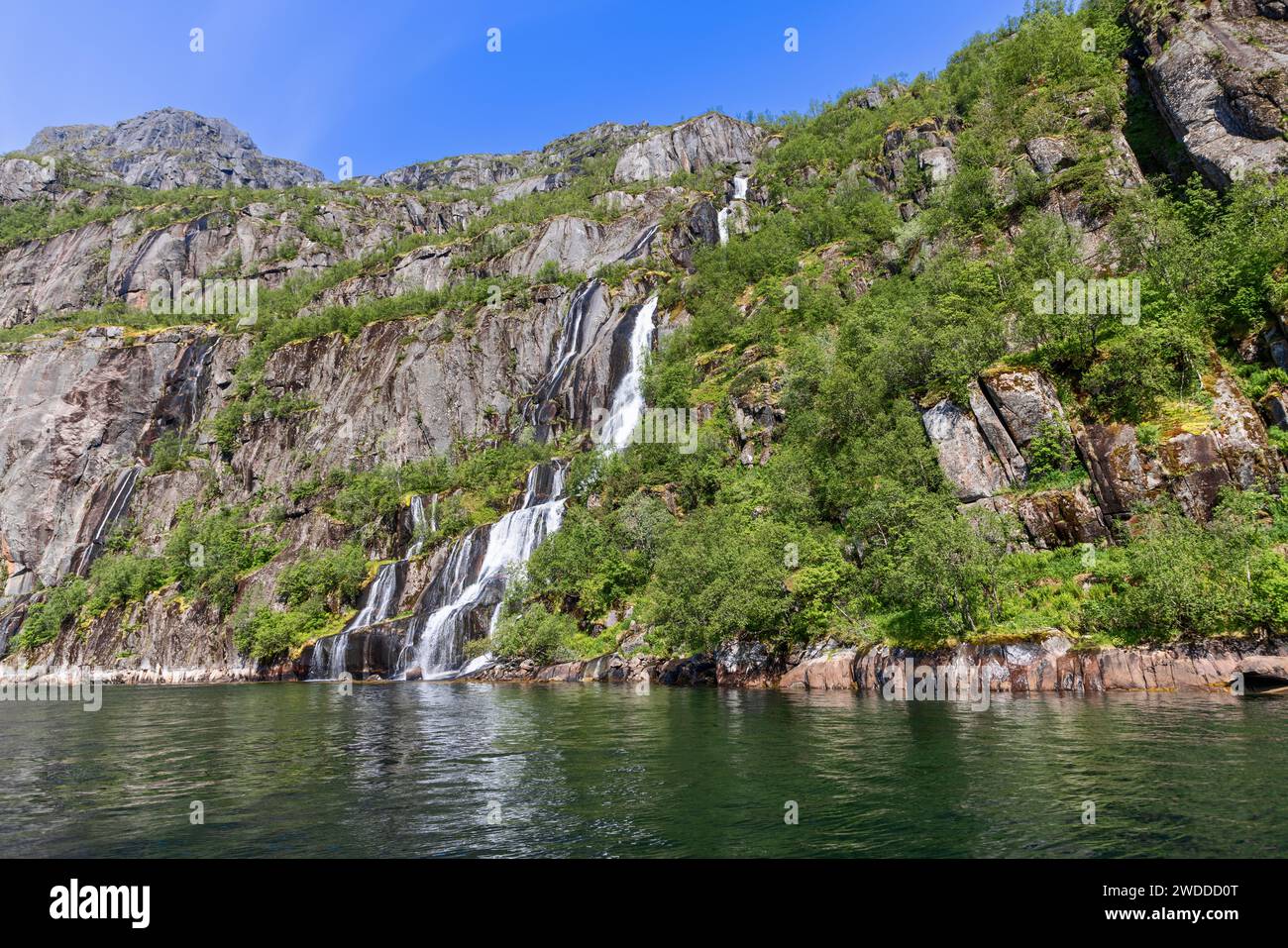 A bright summer day in Lofoten unveils a spectacular waterfall spilling ...