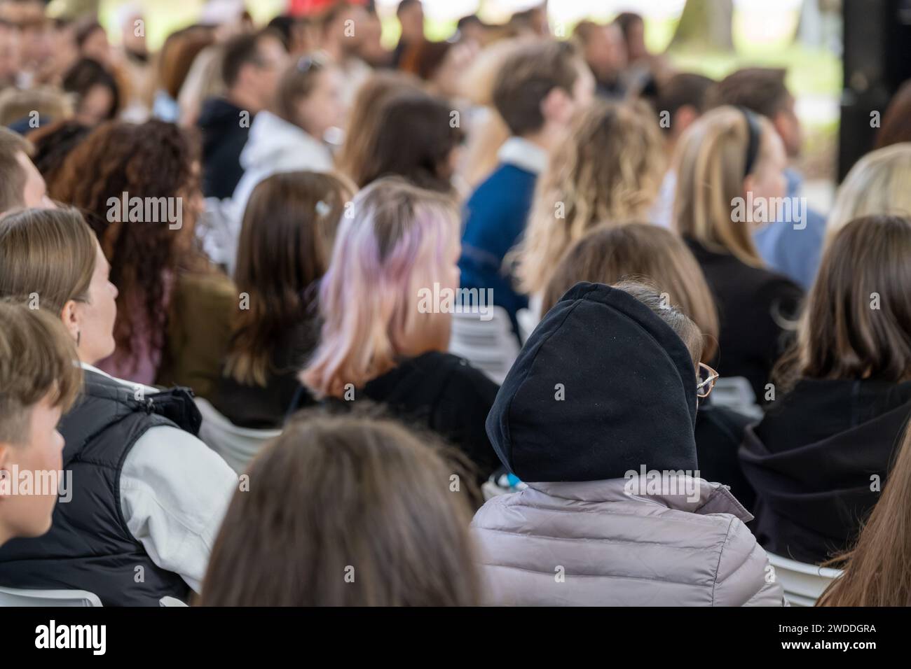 Diverse group of people gathered at an outdoor event, listening ...