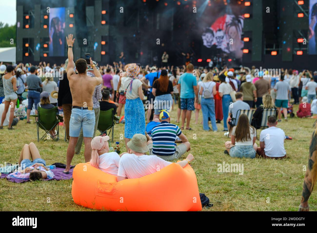 Vibrant crowd at an outdoor festival enjoying a concert with some lying ...