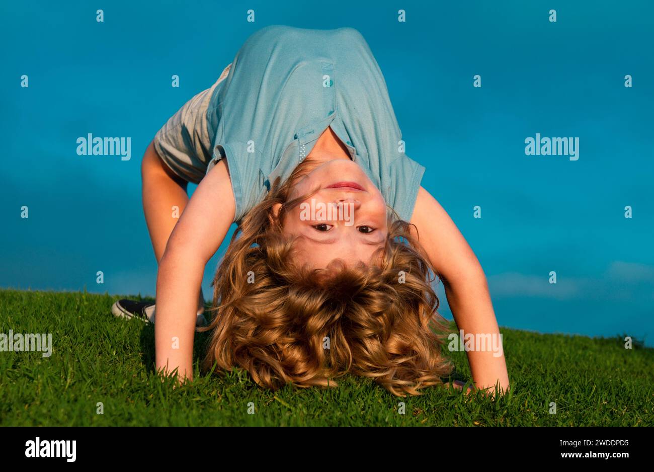 Happy boy doing a headstand on the grass in the summer sunshine. Funny ...