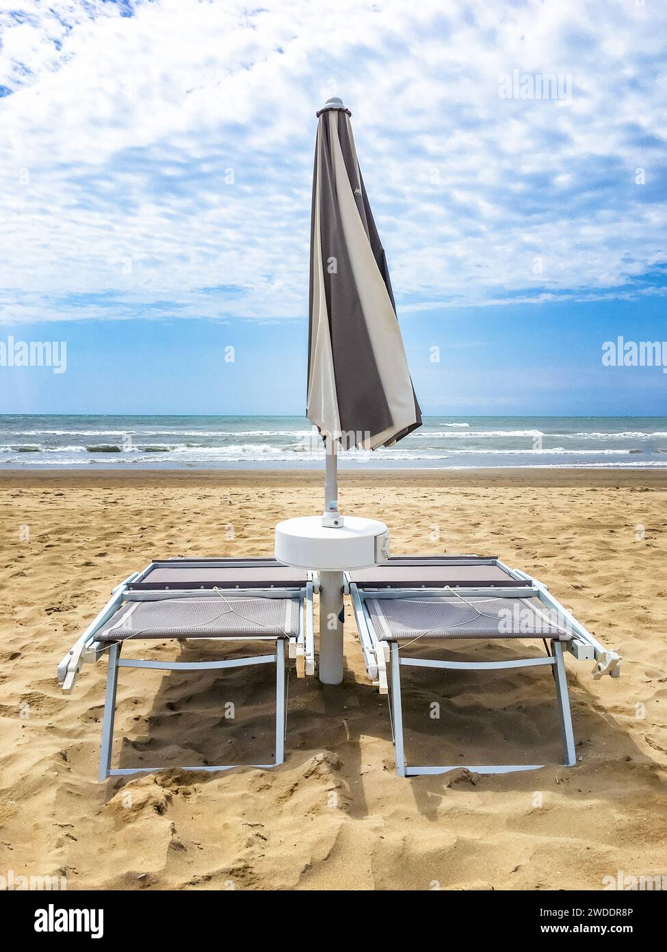 Two sunbeds and an umbrella closed in front of the sea at the end of ...