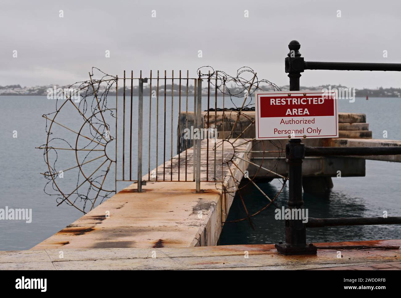 A restricted area sign, in front of a locked gate surrounded by barbed ...