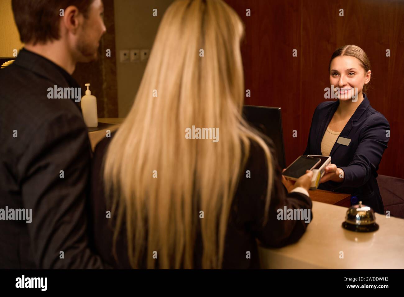 Couple making contactless phone payment over terminal at reception desk ...