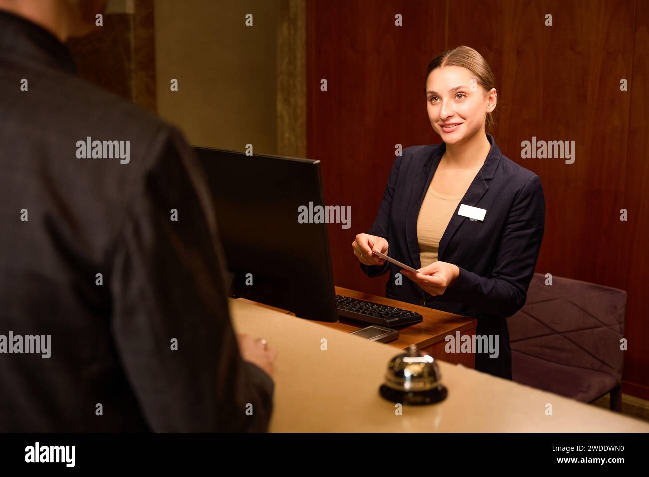 Smiling woman receptionist standing at counter with envelope in hands ...