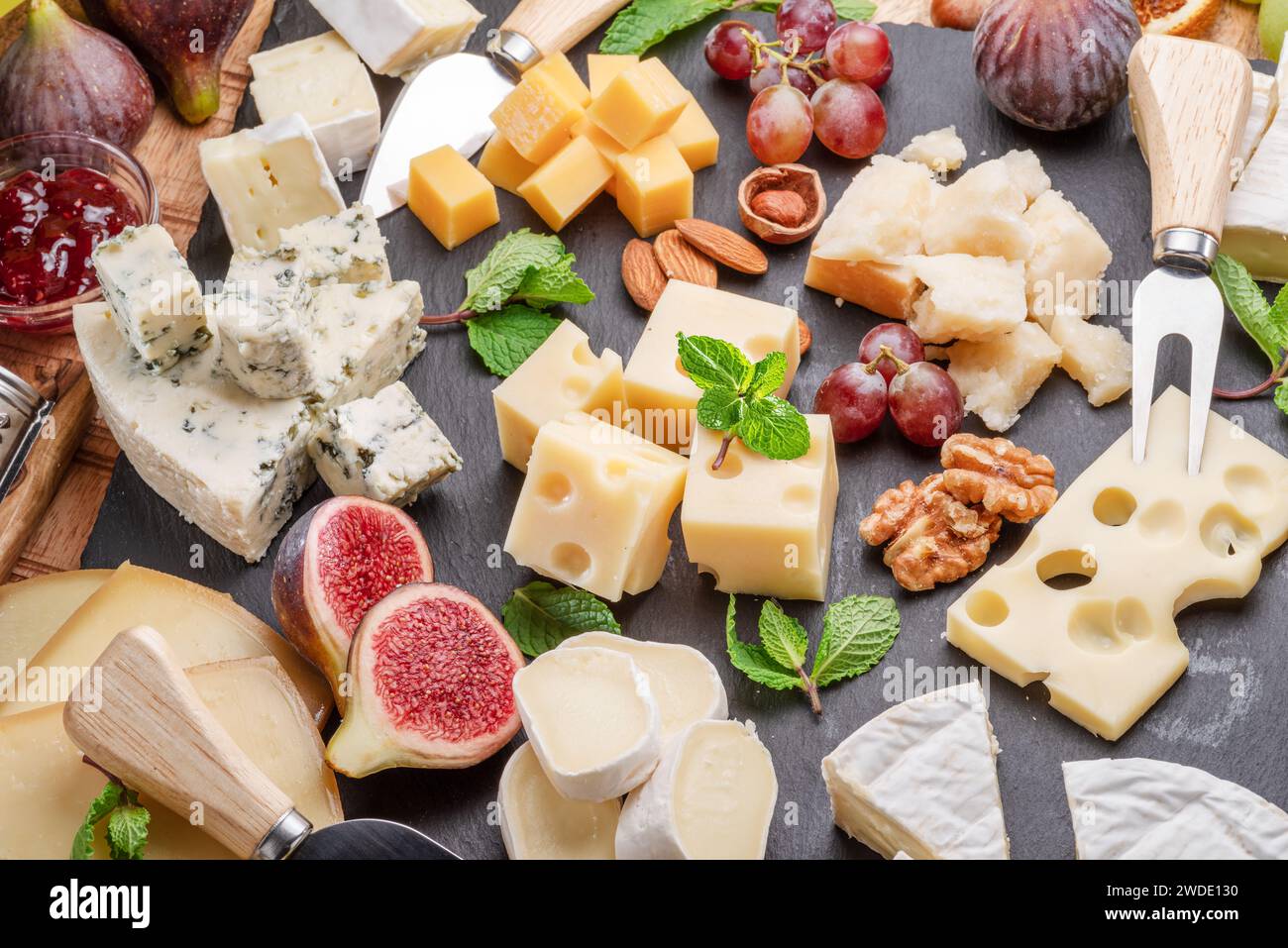 Variety of sliced cheeses with fruits, mint, nuts and cheese cutting ...