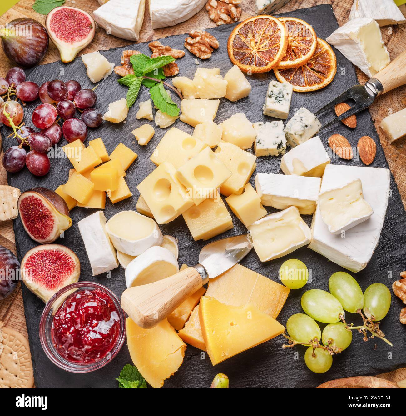 Variety of sliced cheeses with fruits, mint, nuts and cheese cutting ...