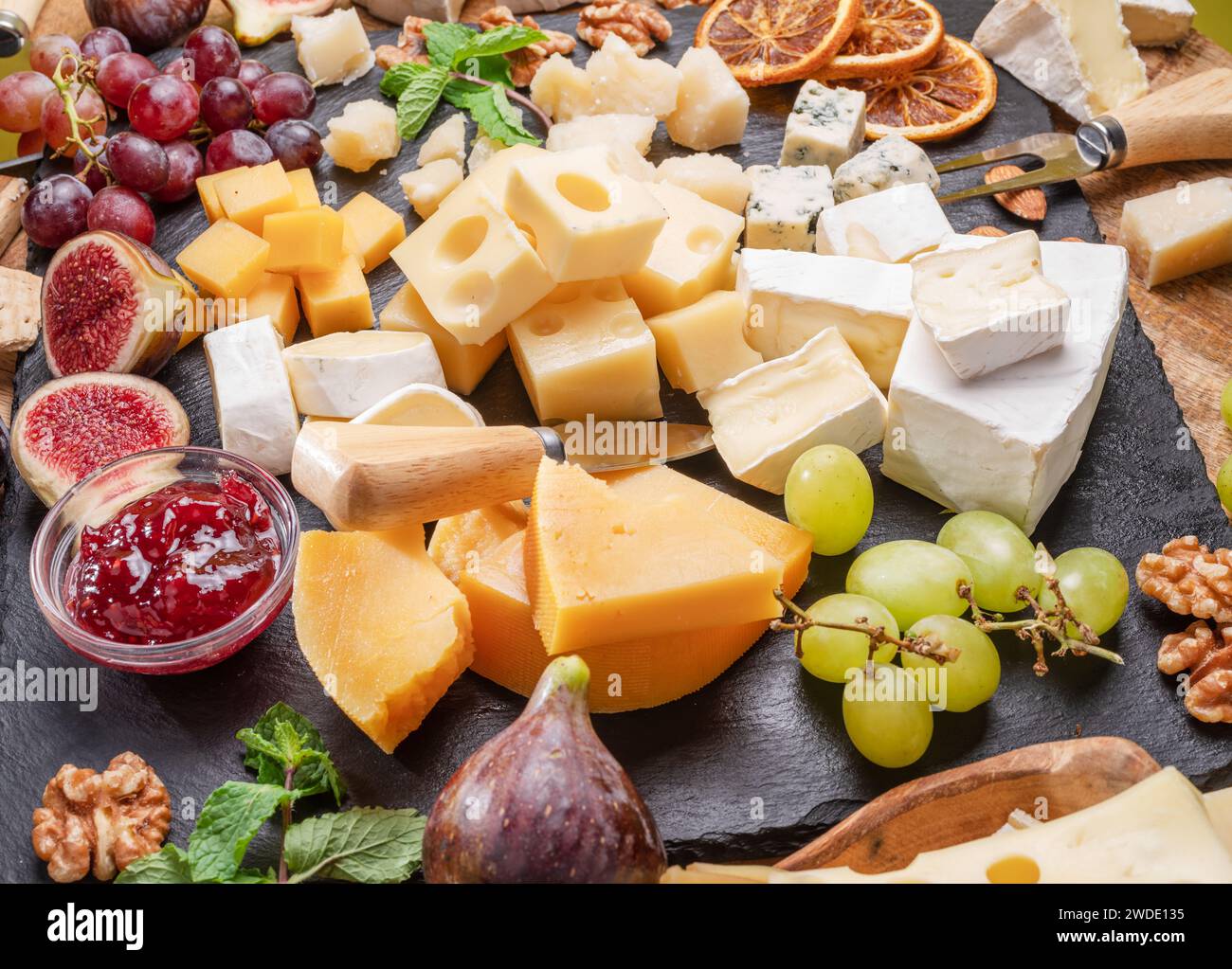 Variety of sliced cheeses with fruits, mint, nuts and cheese cutting ...