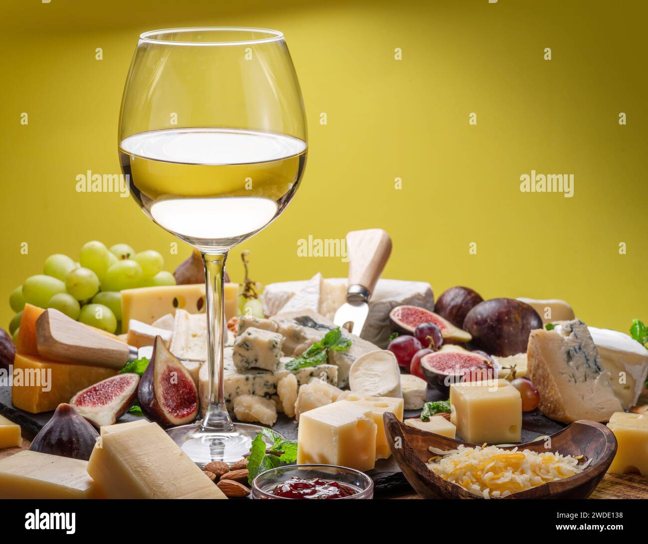 Glass of white wine with variety of sliced cheeses with fruits, mint ...