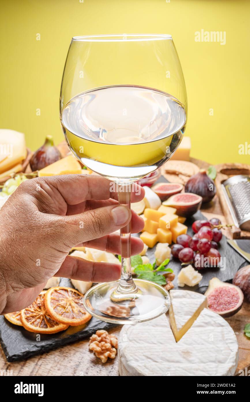 Glass of white wine in a man's hand with variety of sliced cheeses with ...