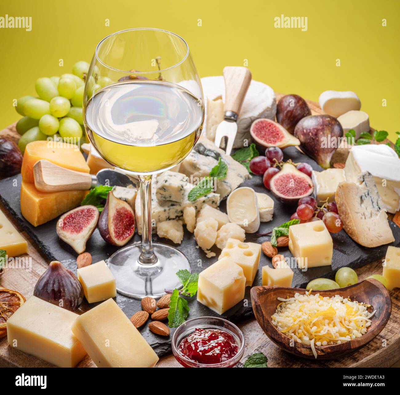 Glass of white wine with variety of sliced cheeses with fruits, mint ...