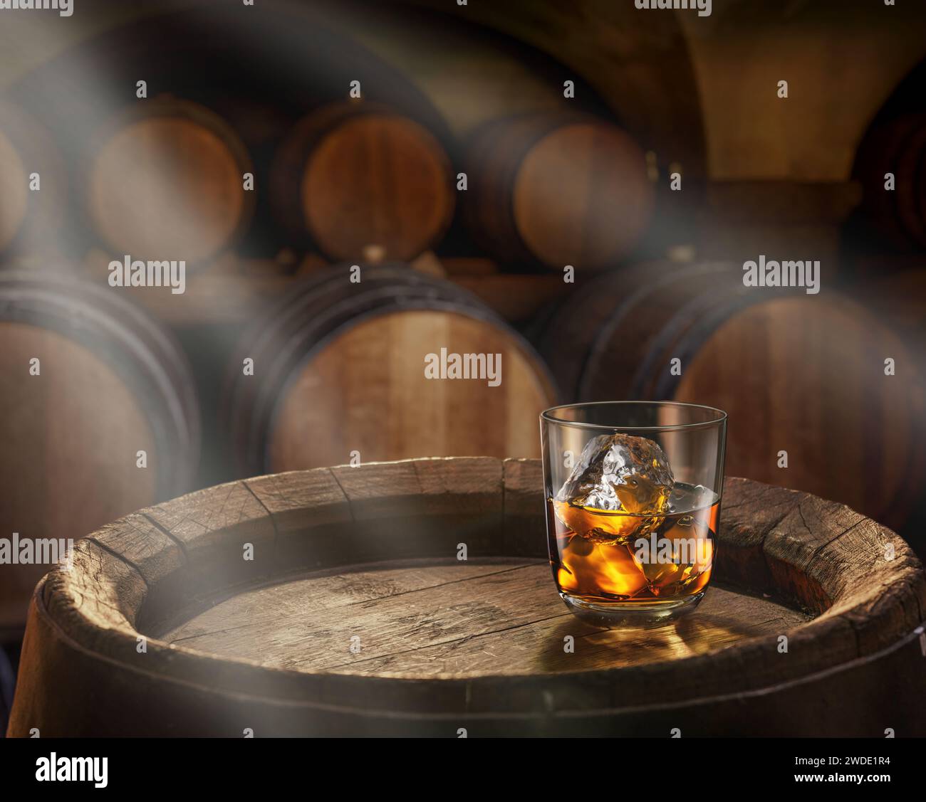 Glass of whiskey on top of wooden barrel and wood barrels in cellar at ...