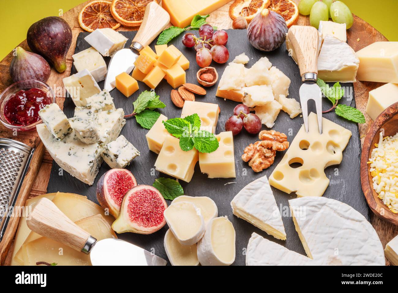 Variety of sliced cheeses with fruits, mint, nuts and cheese cutting ...