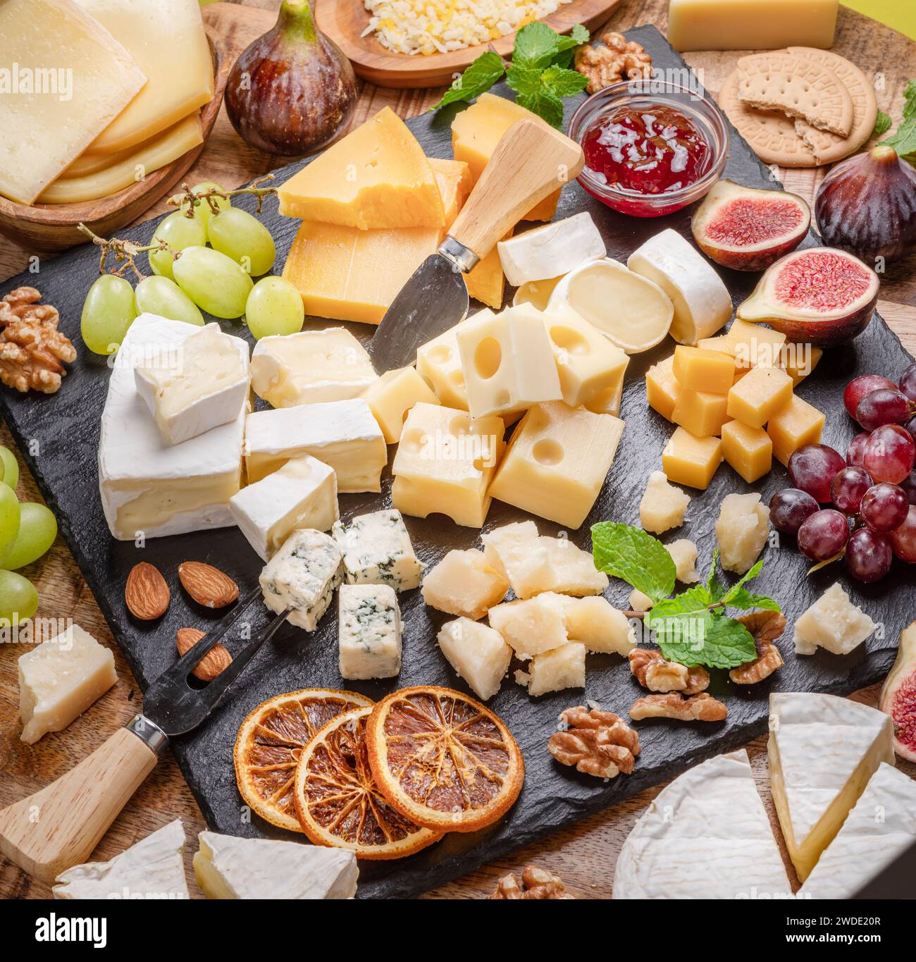 Variety of sliced cheeses with fruits, mint, nuts and cheese cutting ...