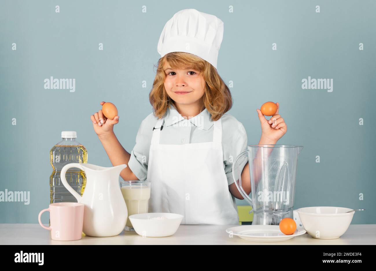Child chef isolated on blue hold eggs. Funny little kid chef cook ...