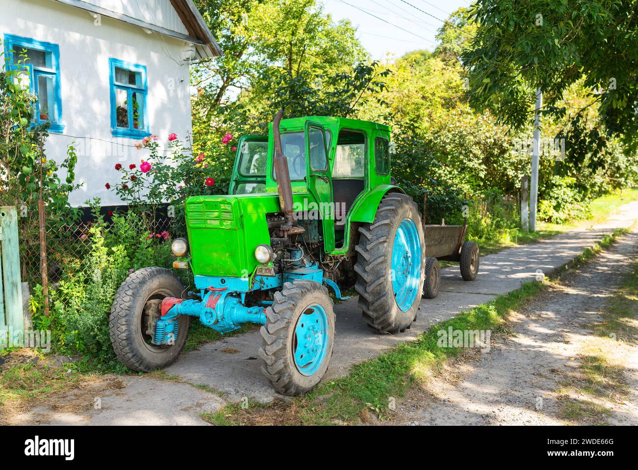 A green vintage tractor is parked in front of a white house with blue ...
