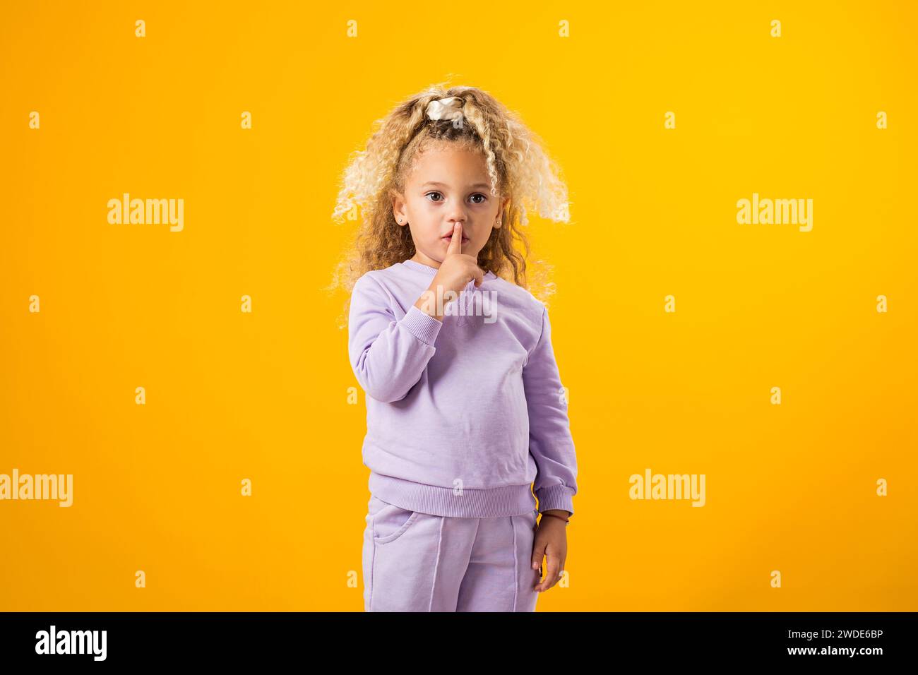 Portrait of child girl touching her lips with finger, demonstrate shh ...