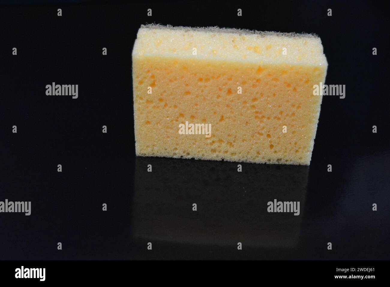 On a black glossy background, a kitchen sponge is laid and lies, a ...