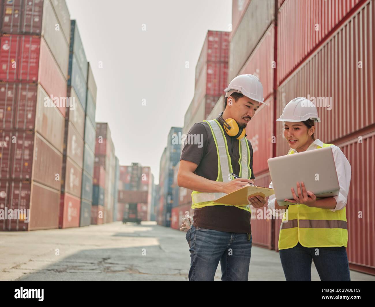 young Asian woman and man engineer working with co-worker at overseas shipping container yard ...